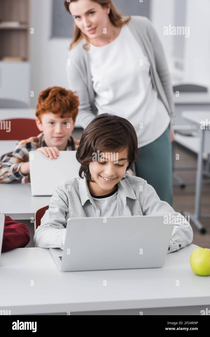 teacher standing near pupils using laptops during lesson, blurred ...