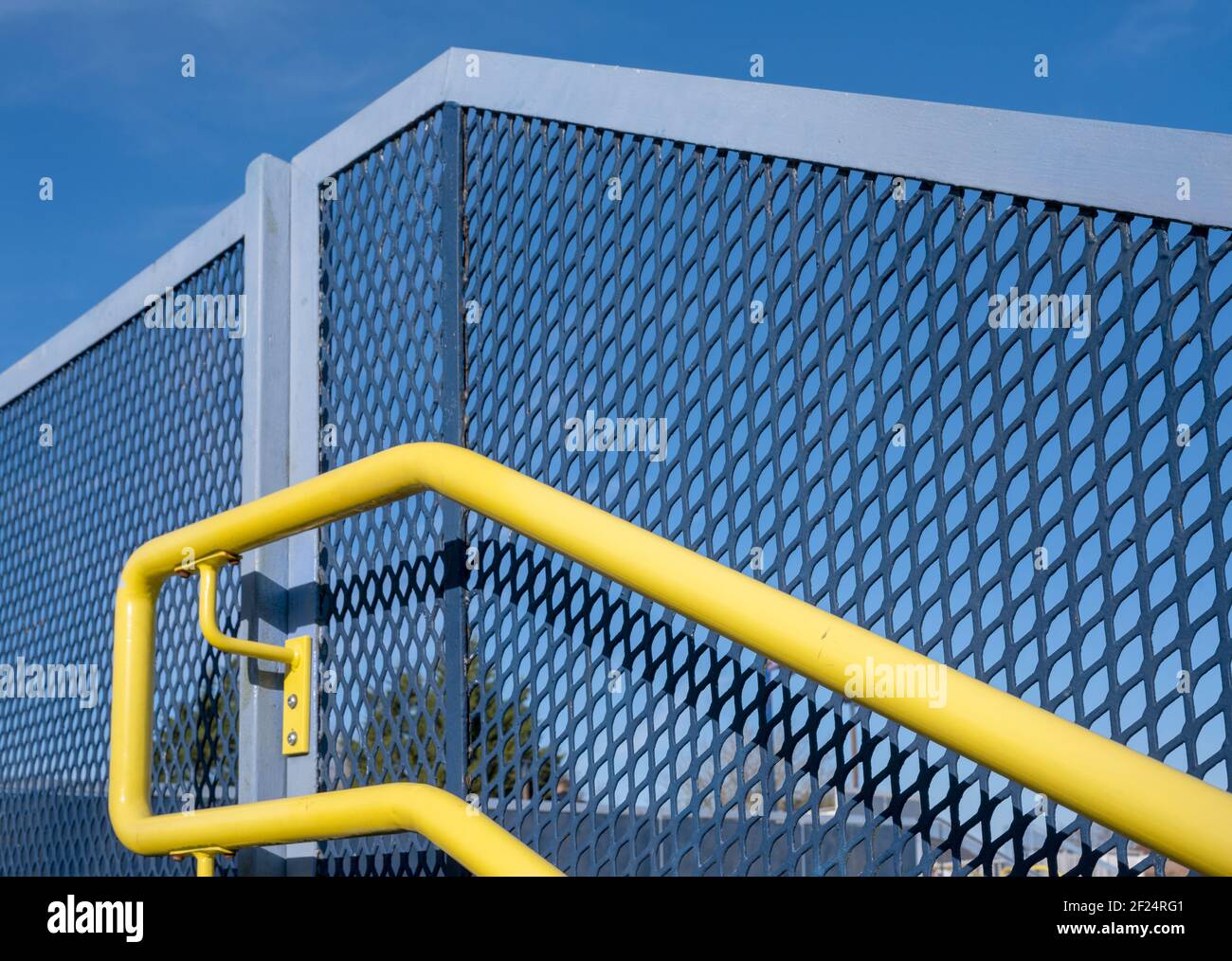 Yellow handrail against a blue meshed fence Stock Photo - Alamy