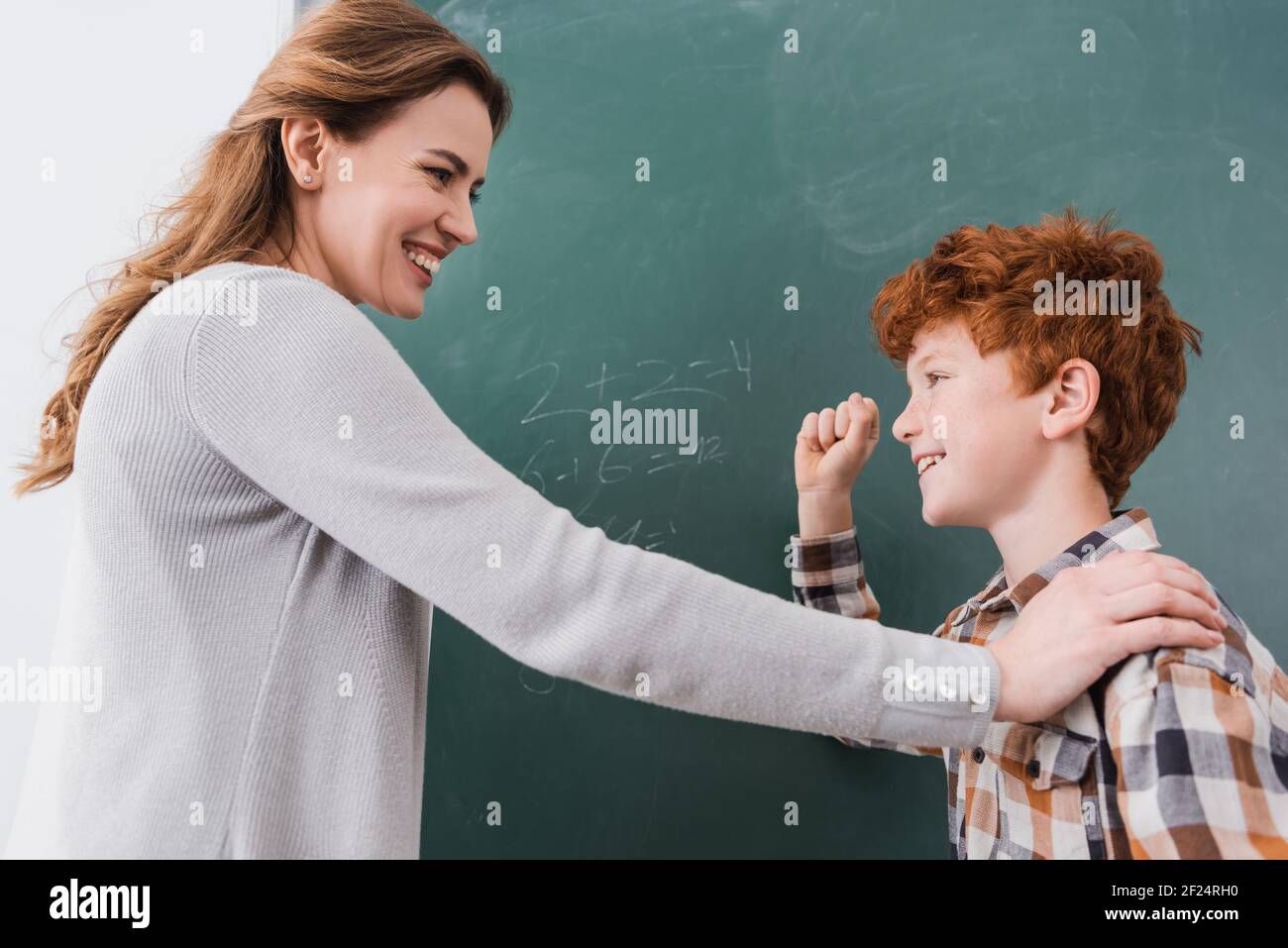 smiling teacher touching shoulder of schoolboy showing win gesture near ...