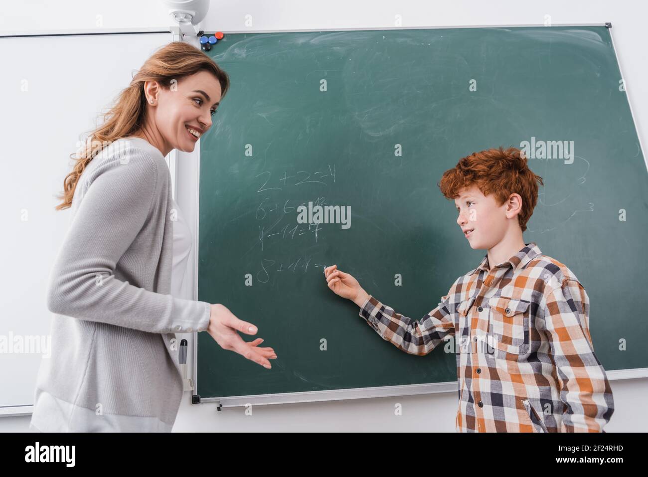 smiling teacher and redhead schoolboy looking at each other near ...