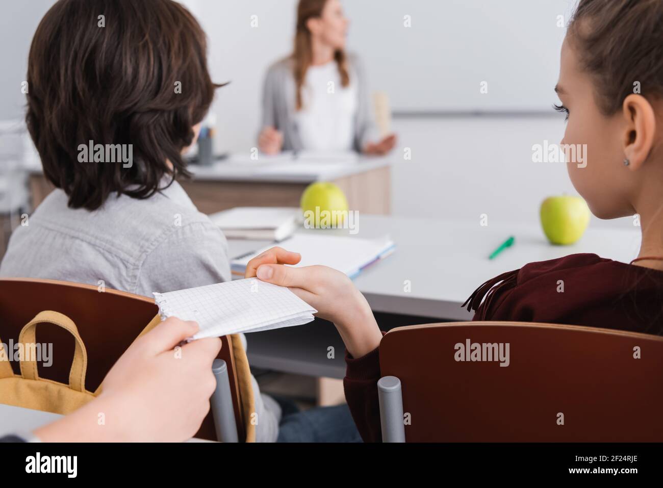 kid passing message to schoolgirl near teacher on blurred background ...
