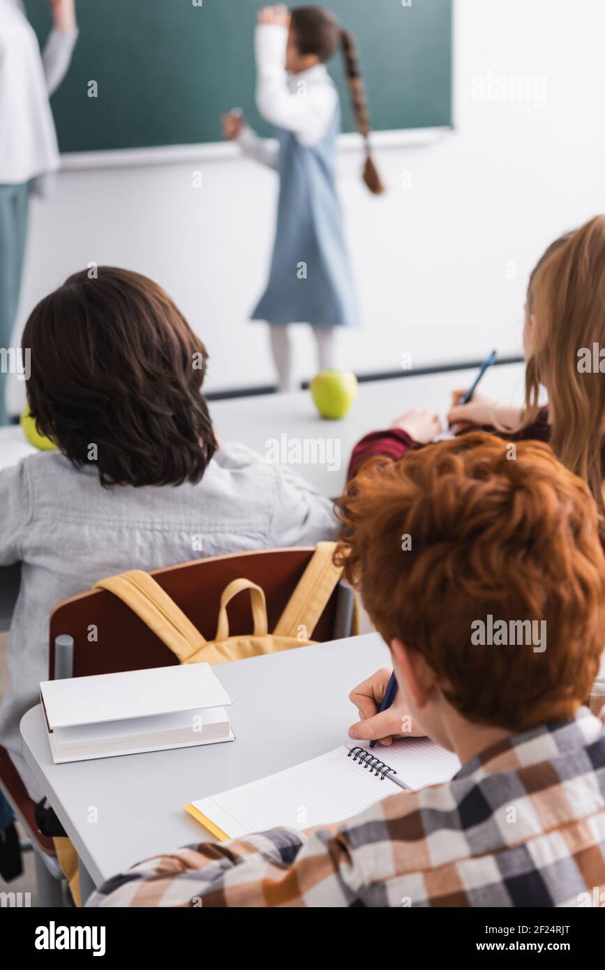 back view of pupils writing during lesson in classroom, blurred ...