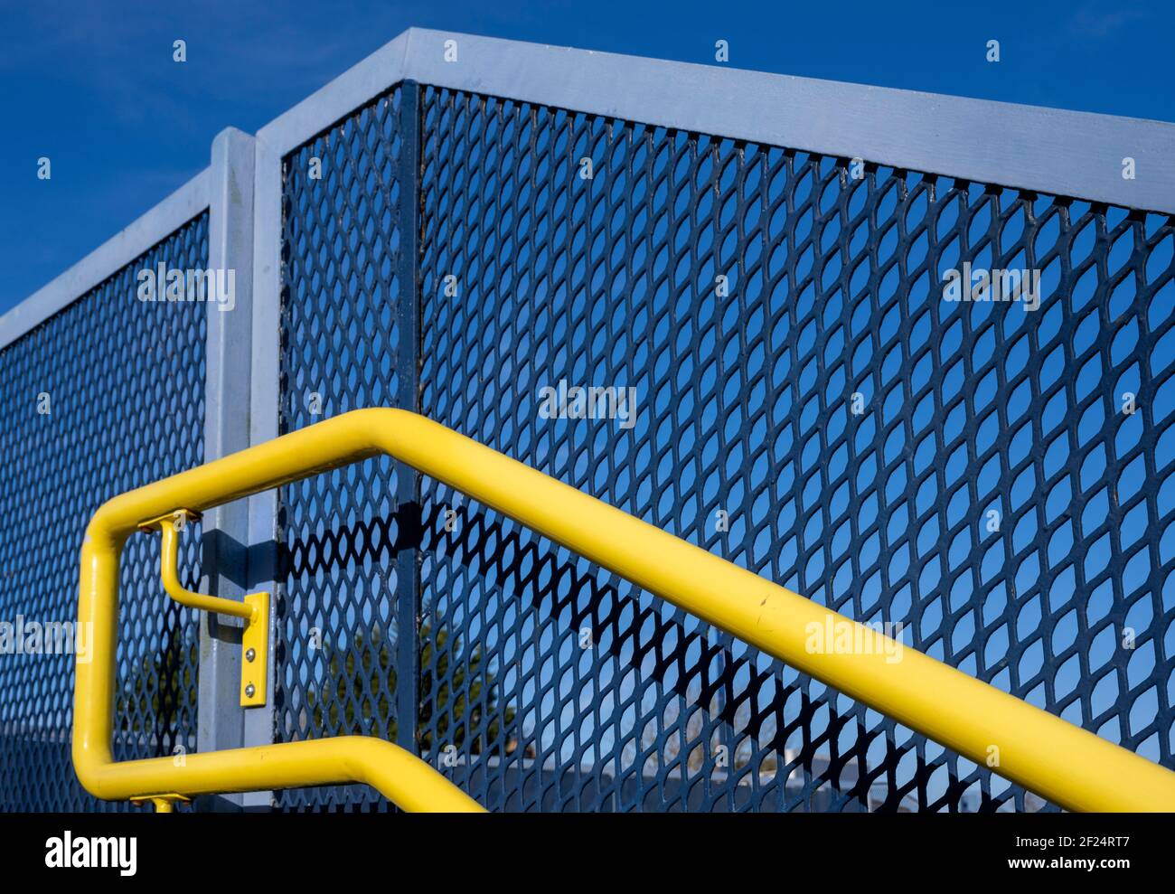 Yellow handrail against a blue meshed fence Stock Photo - Alamy