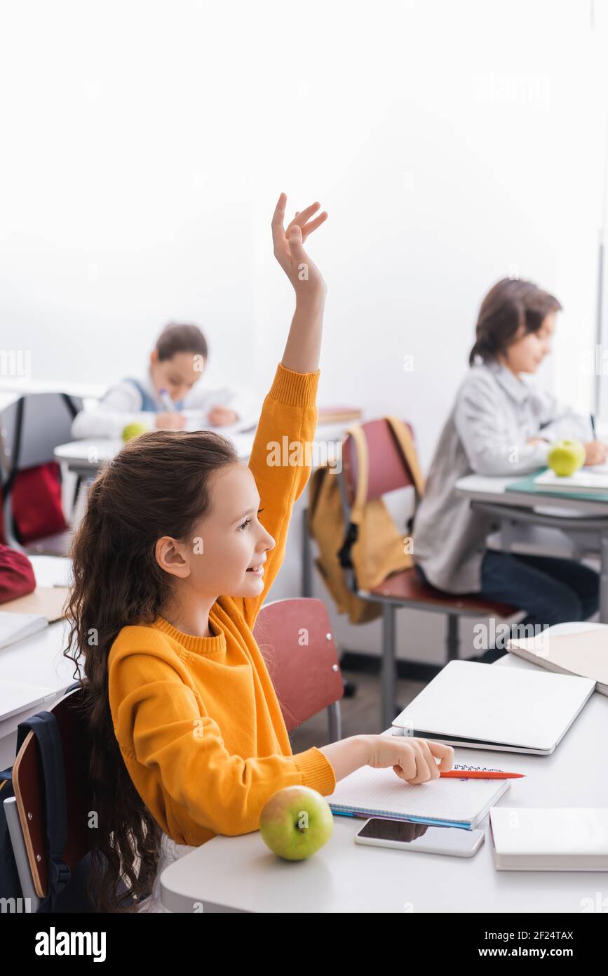 Smiling kid raising hand near devices, apple and notebook on school ...