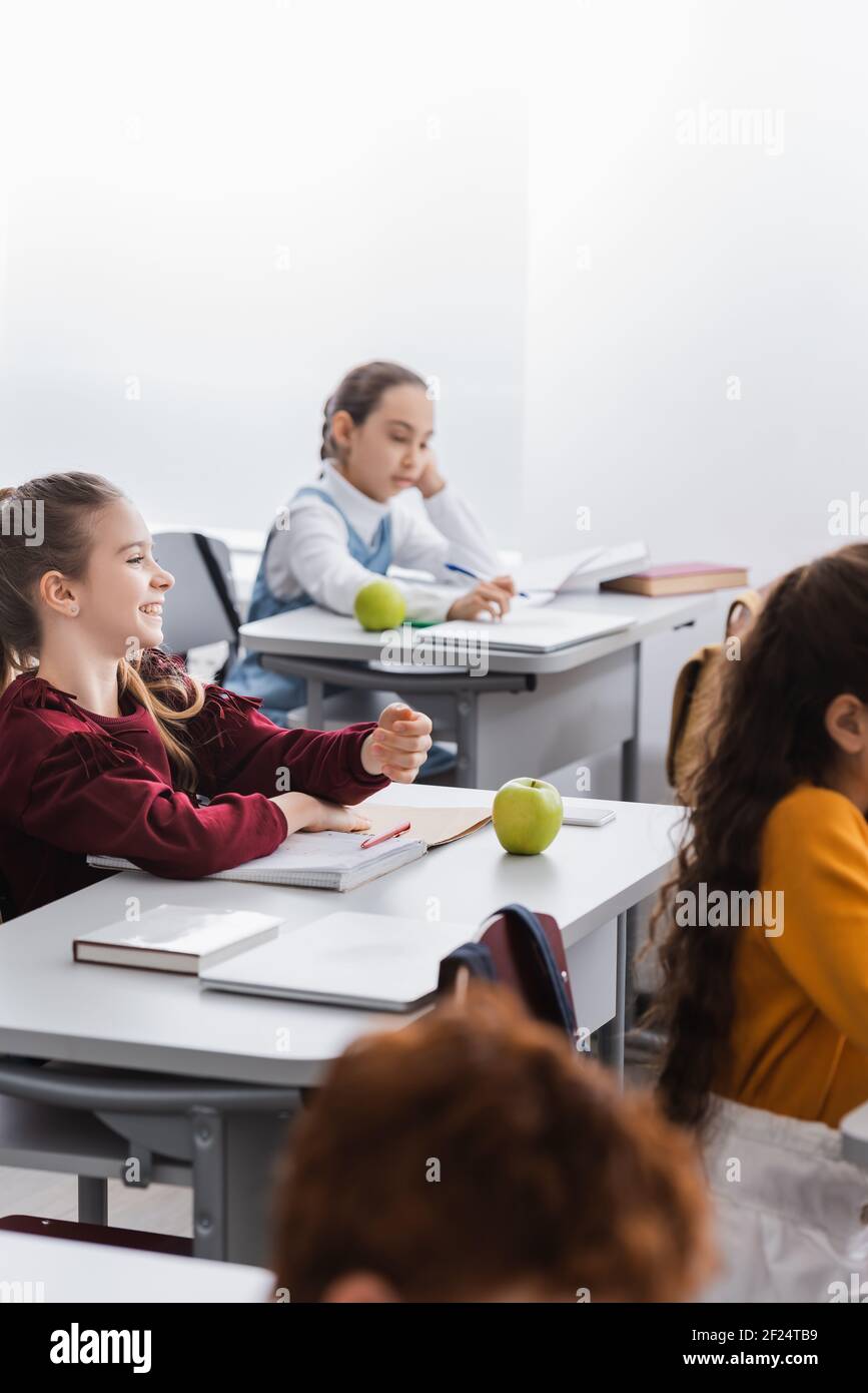 Positive pupil sitting near notebook and devices on desk in classroom ...
