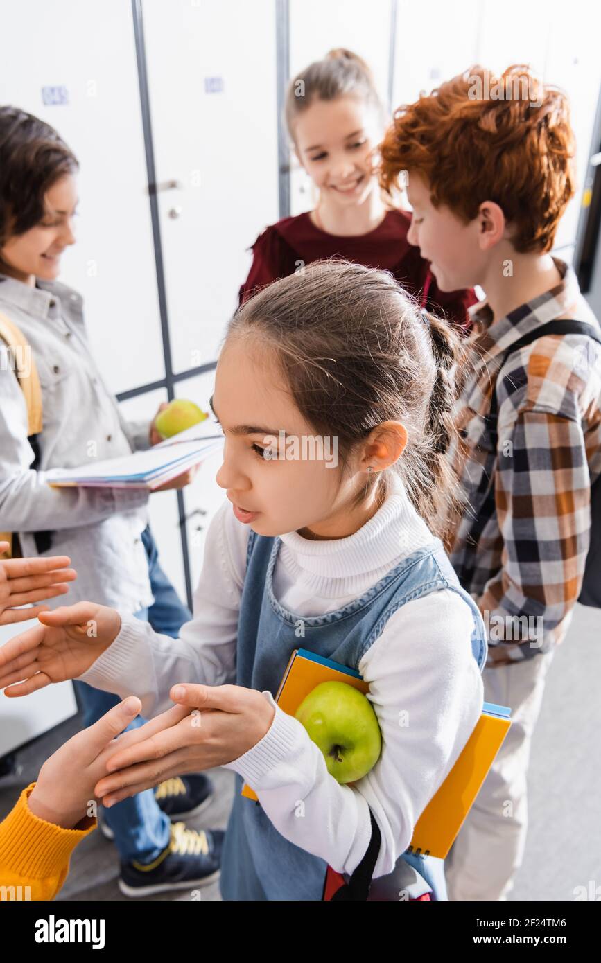 Schoolgirl with apple and notebook playing patty cake game with friend ...