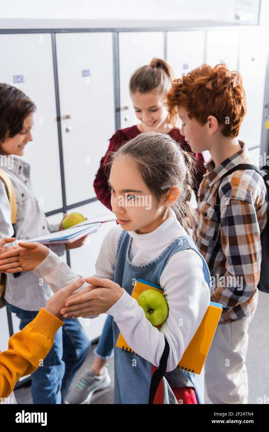 Schoolkids with apples and notebooks playing patty cake game in hall of ...
