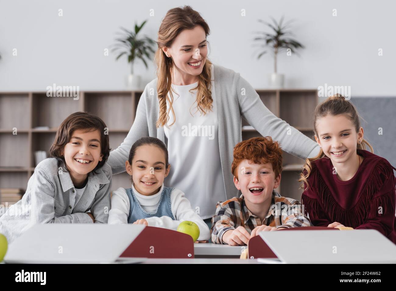 cheerful classmates smiling at camera near happy teacher in school ...