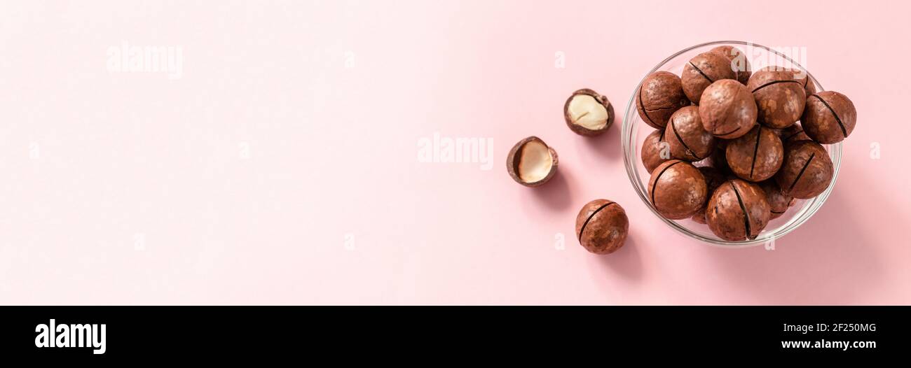 Raw macadamia nuts in a transparent glass bowl and scattered on pink ...