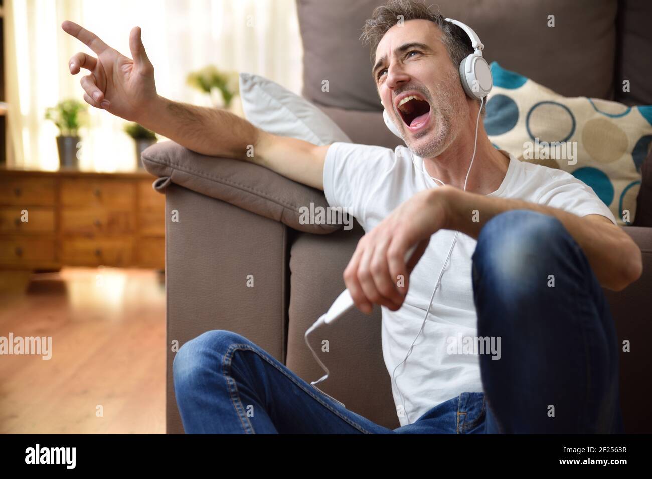 Man sitting on the floor leaning on a sofa listening to music from ...