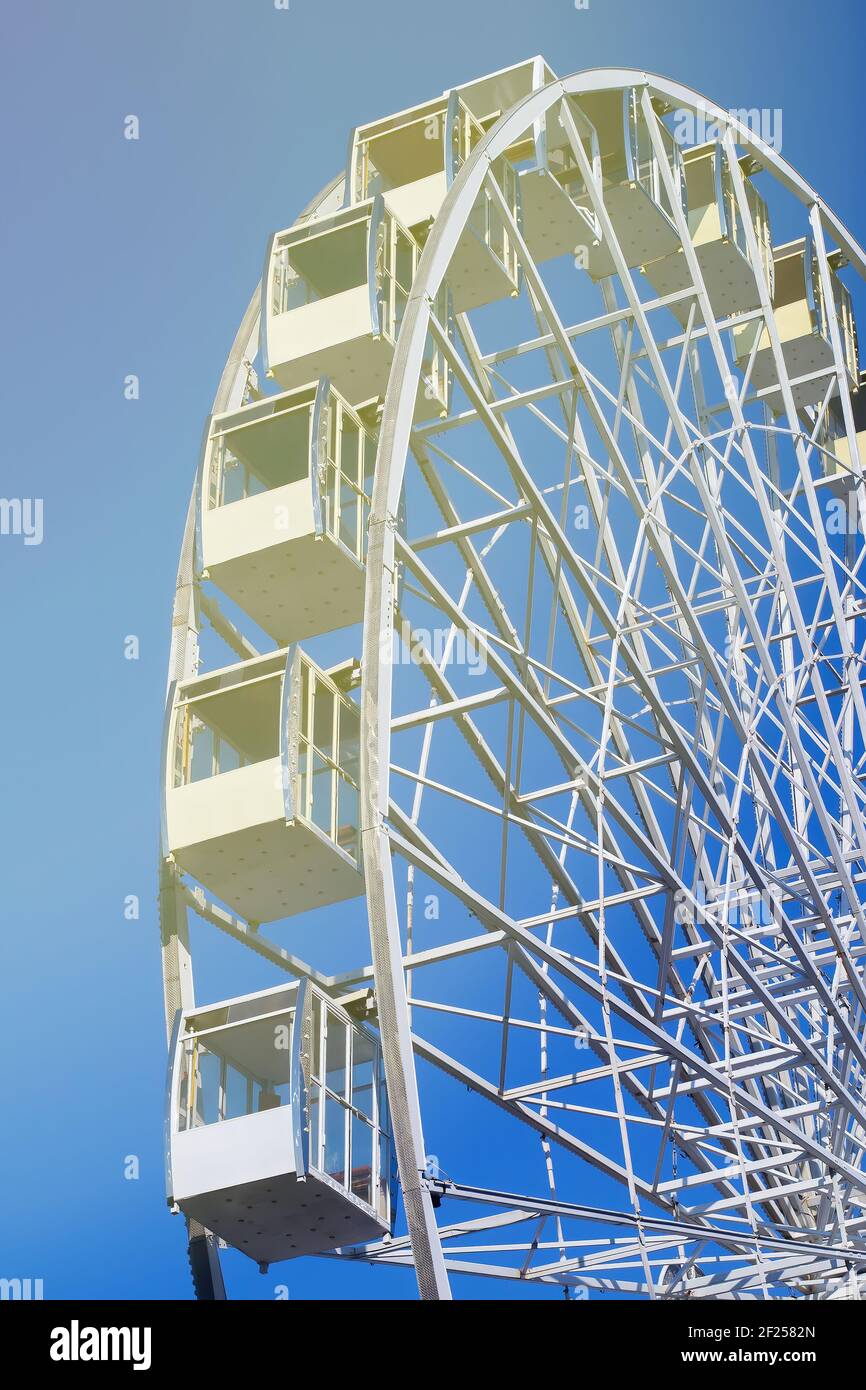 Modern white Ferris wheel with closed glass booths against a blue sky ...