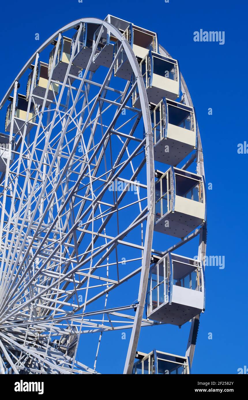 Modern white ferris wheel with closed glass booths against the blue sky ...
