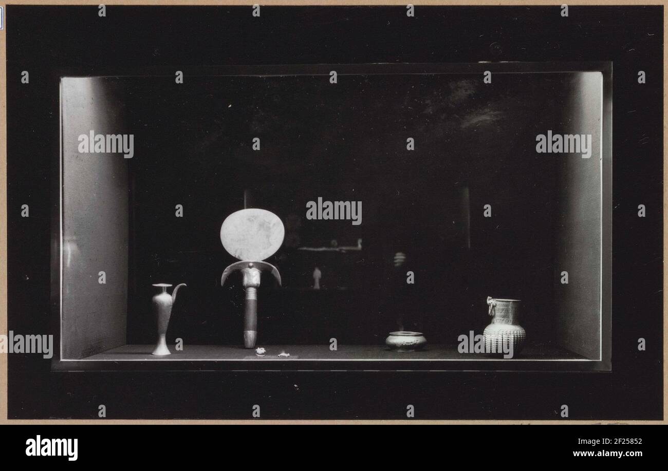 Showcase with various objects including a vase, a can and a mirror ...