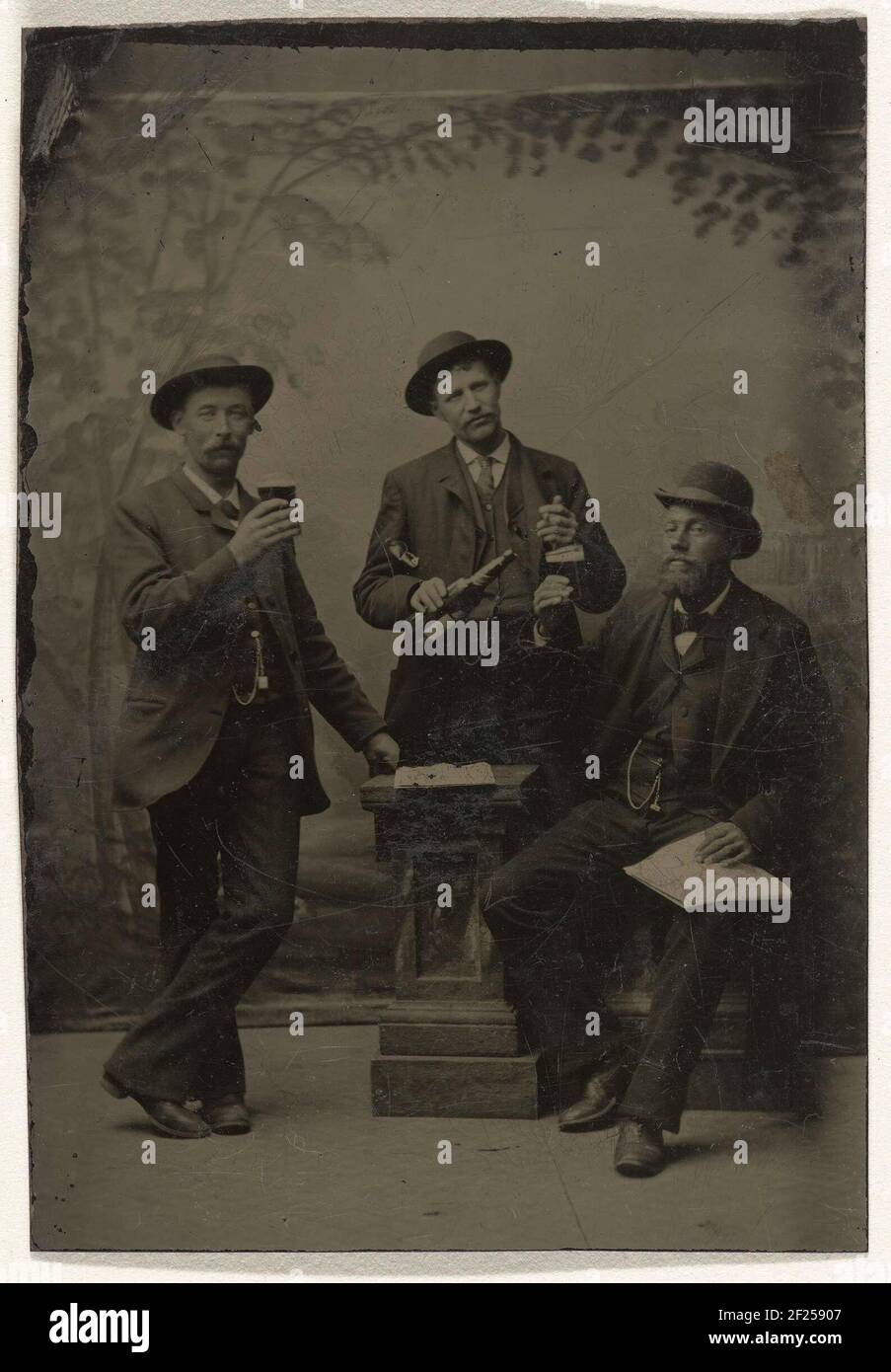 Portrait of three men with bottle and glasses, standing and sitting in ...