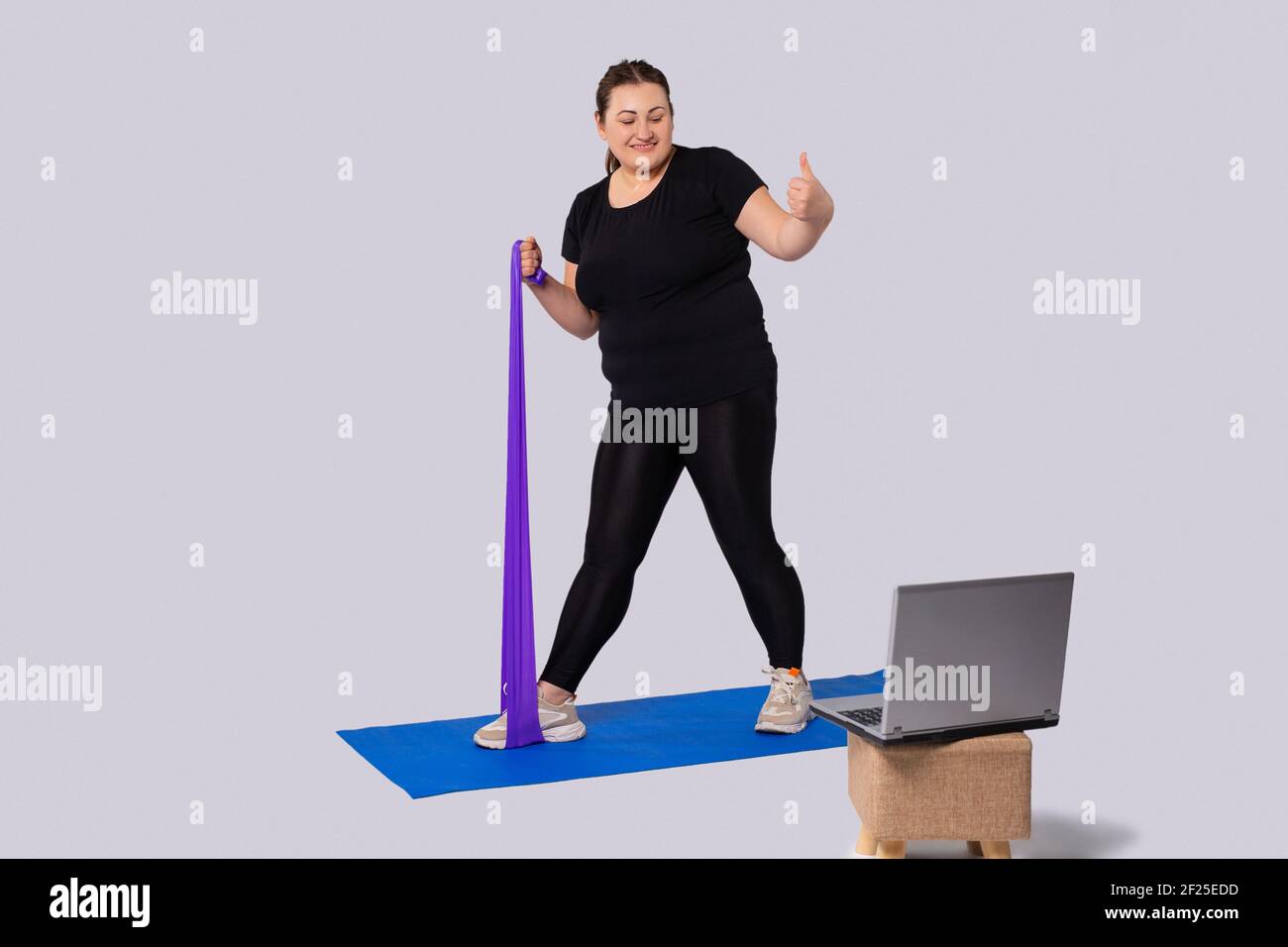A swift plus size woman is doing exercises with a fitness rubber band ...