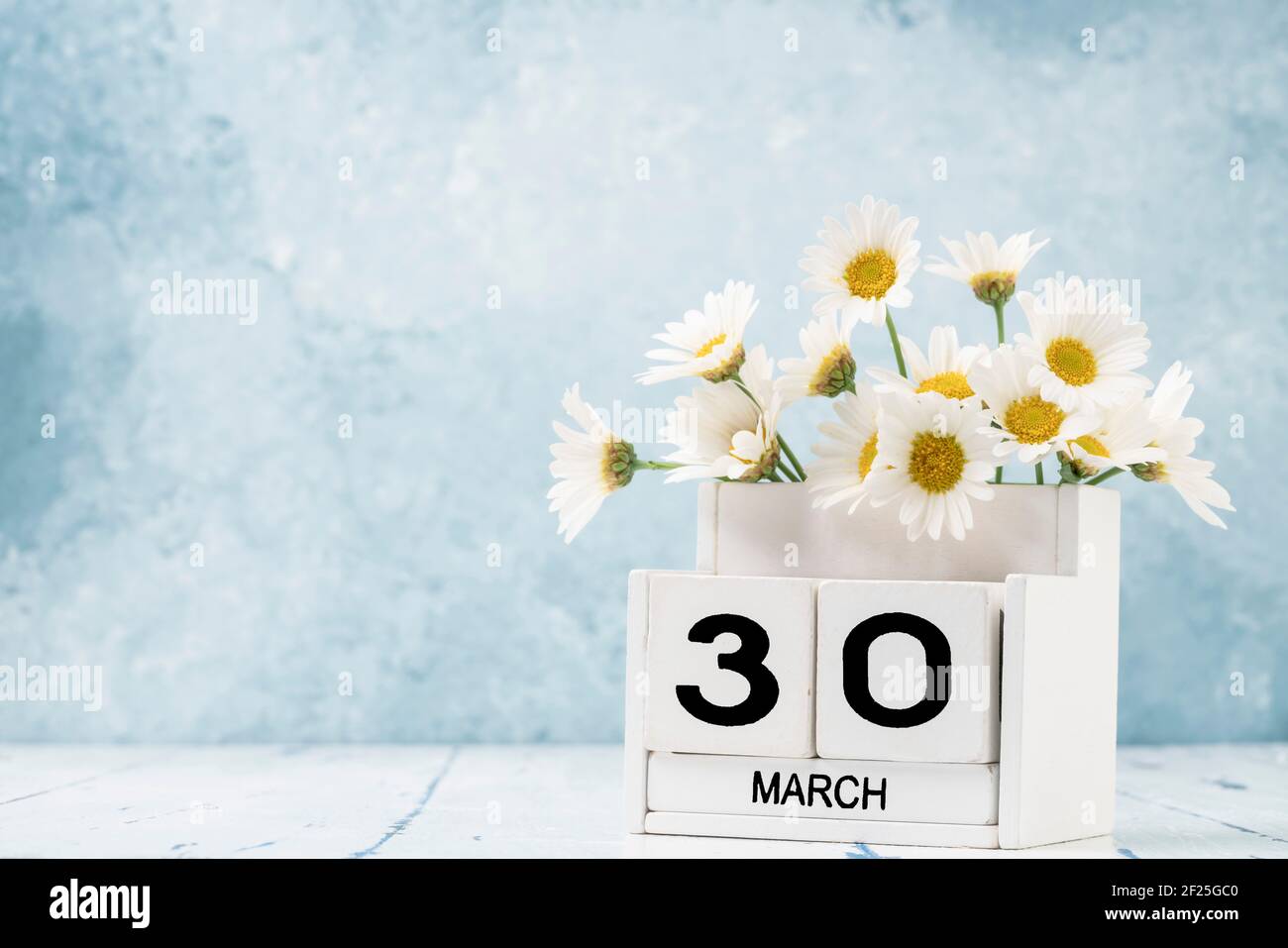 White cube calendar for march decorated with daisy flowers over blue ...