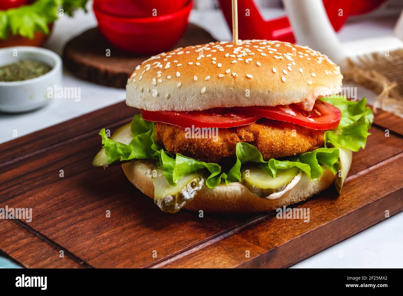 side view chicken burger with sliced tomato and lettuce on the board ...