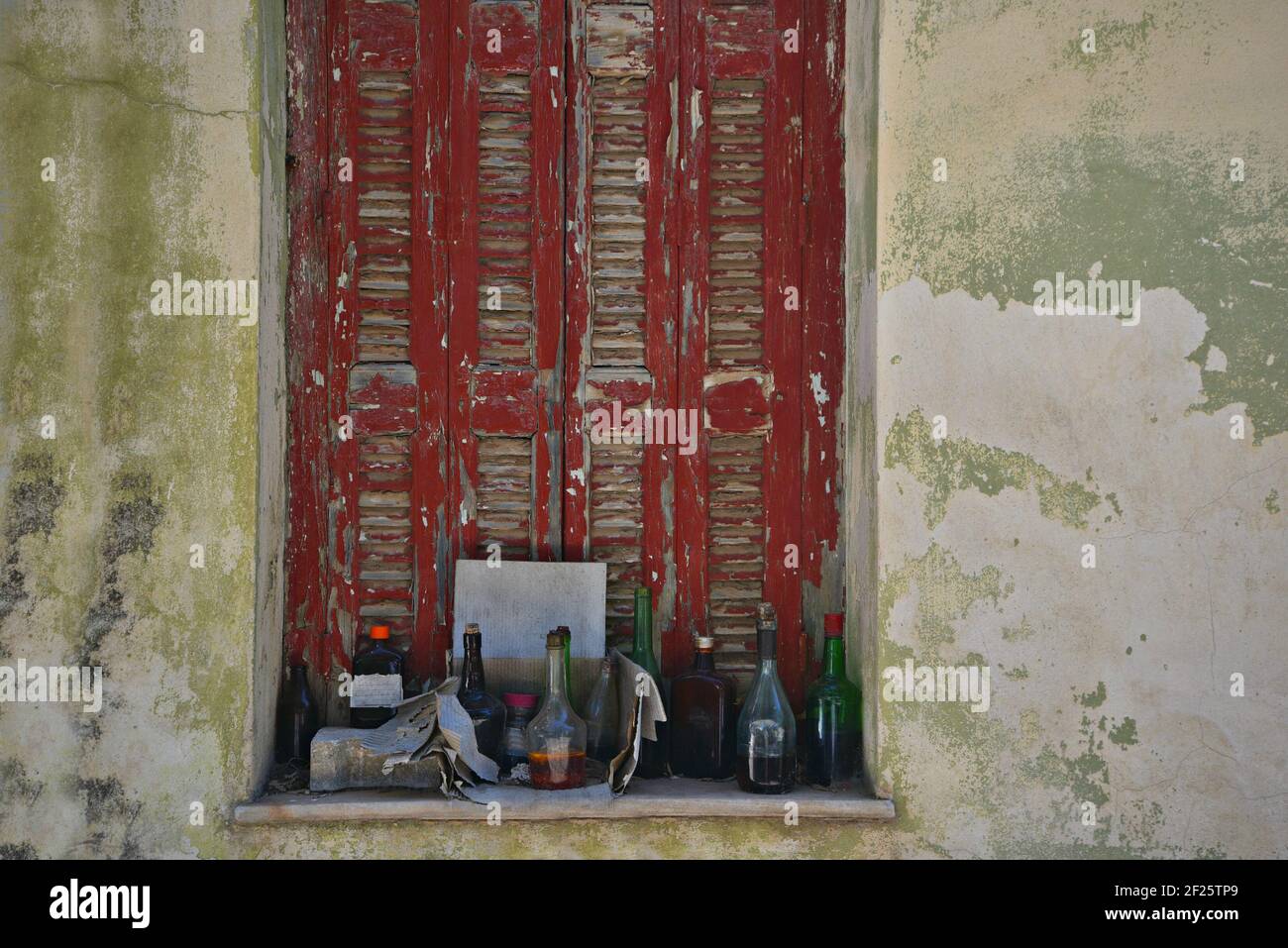 Antique window with red weathered shutters and empty liquor bottles on ...