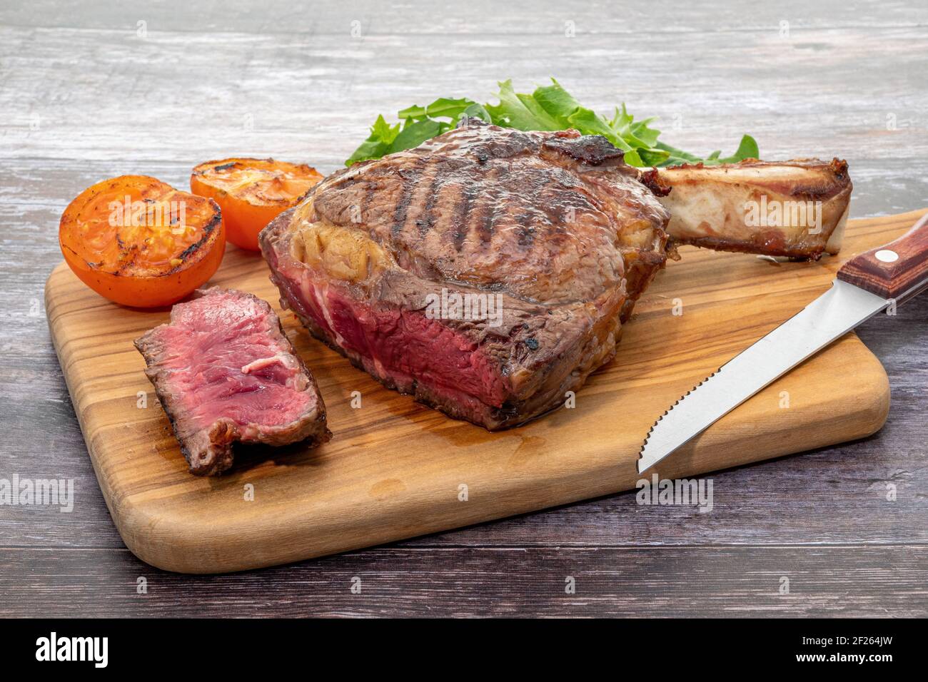 A grilled rib eye tomahawk steak cooked rare on a wooden cutting board ...
