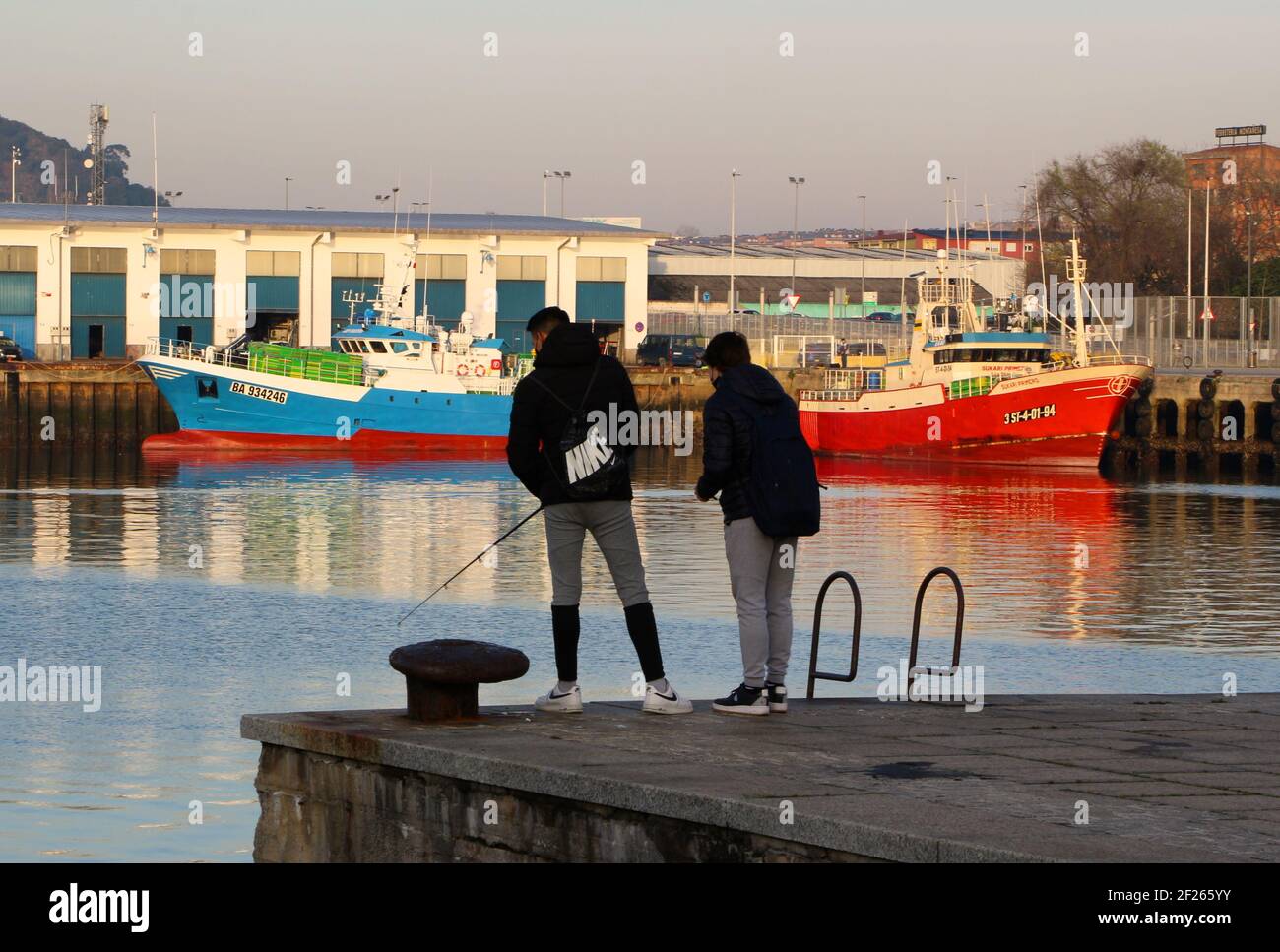 Two young men fishing in the Maliano Dock with the Cap Finistere french ...