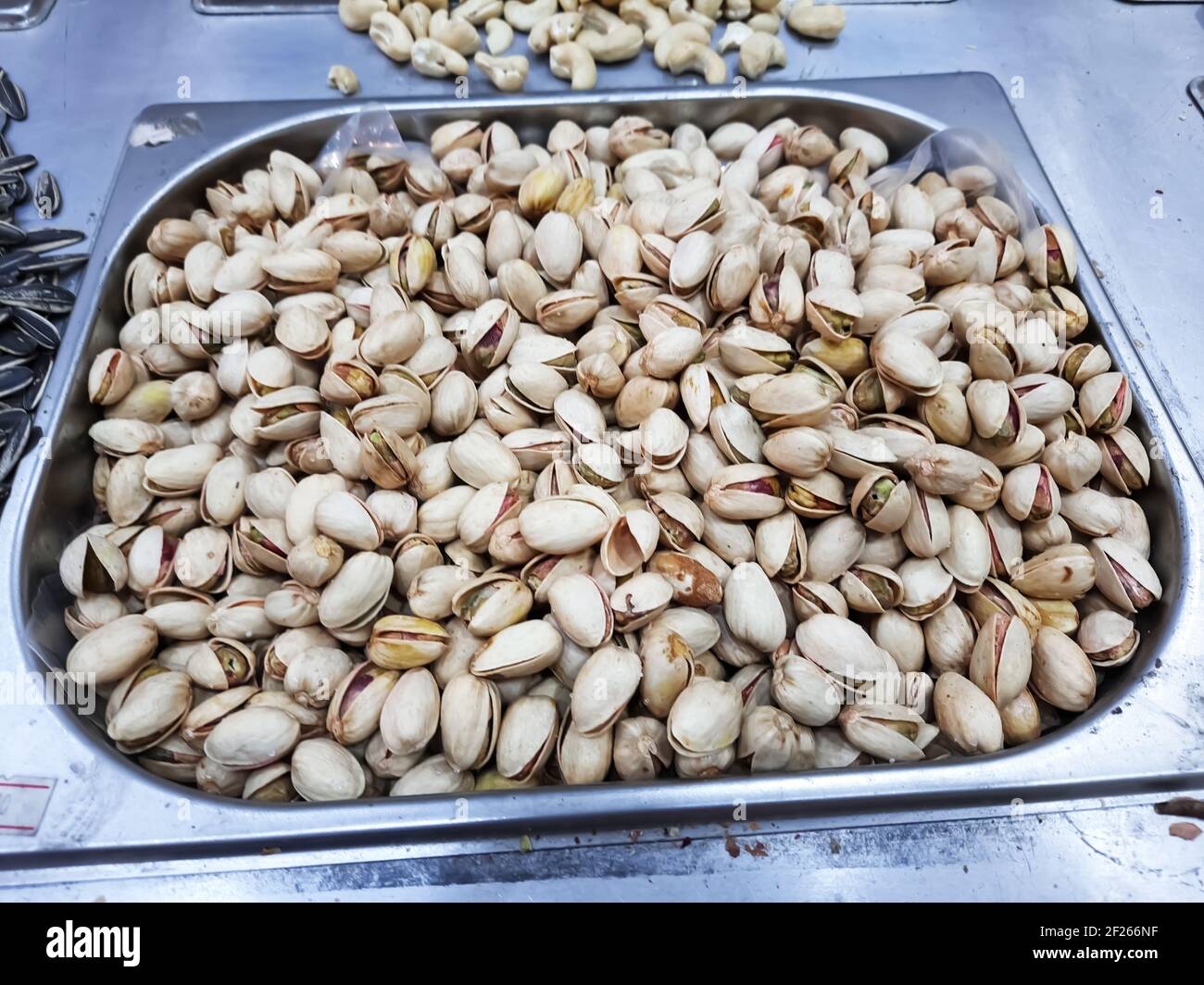 A shot of lots of pistachio cashew seeds in shells in a metal square ...
