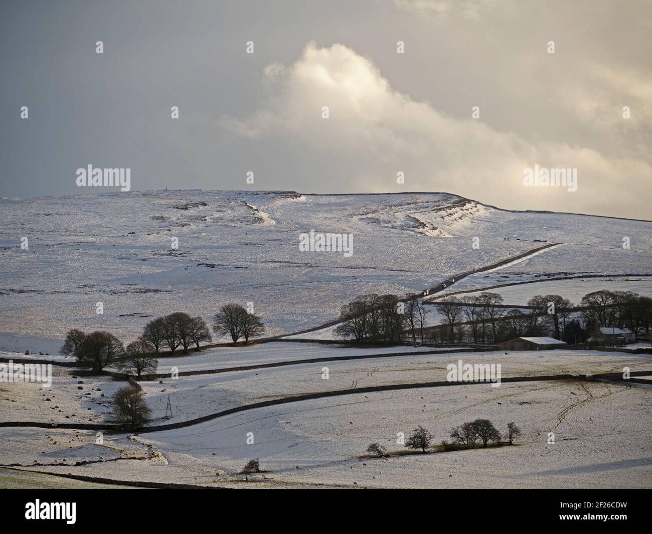 Sunlight on exposed rocky limestone scar above bare trees & farmland ...