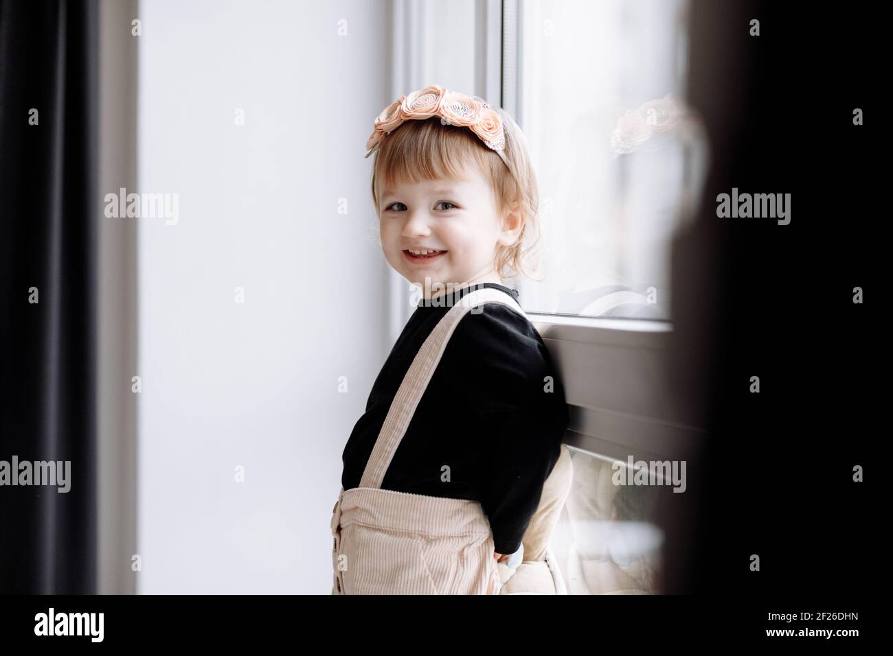 Cute little 2 years old girl standing and looking in large window ...