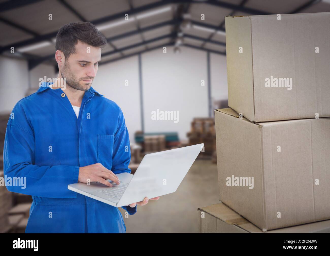 Composition of warehouse worker using laptop over stack of cardboard ...