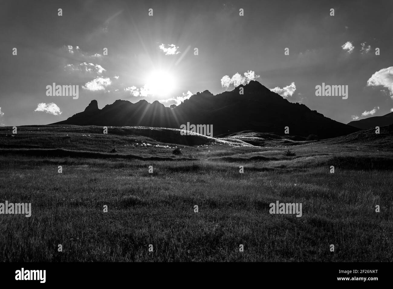 A grayscale shot of a landscape with the bright sun over the mountains ...
