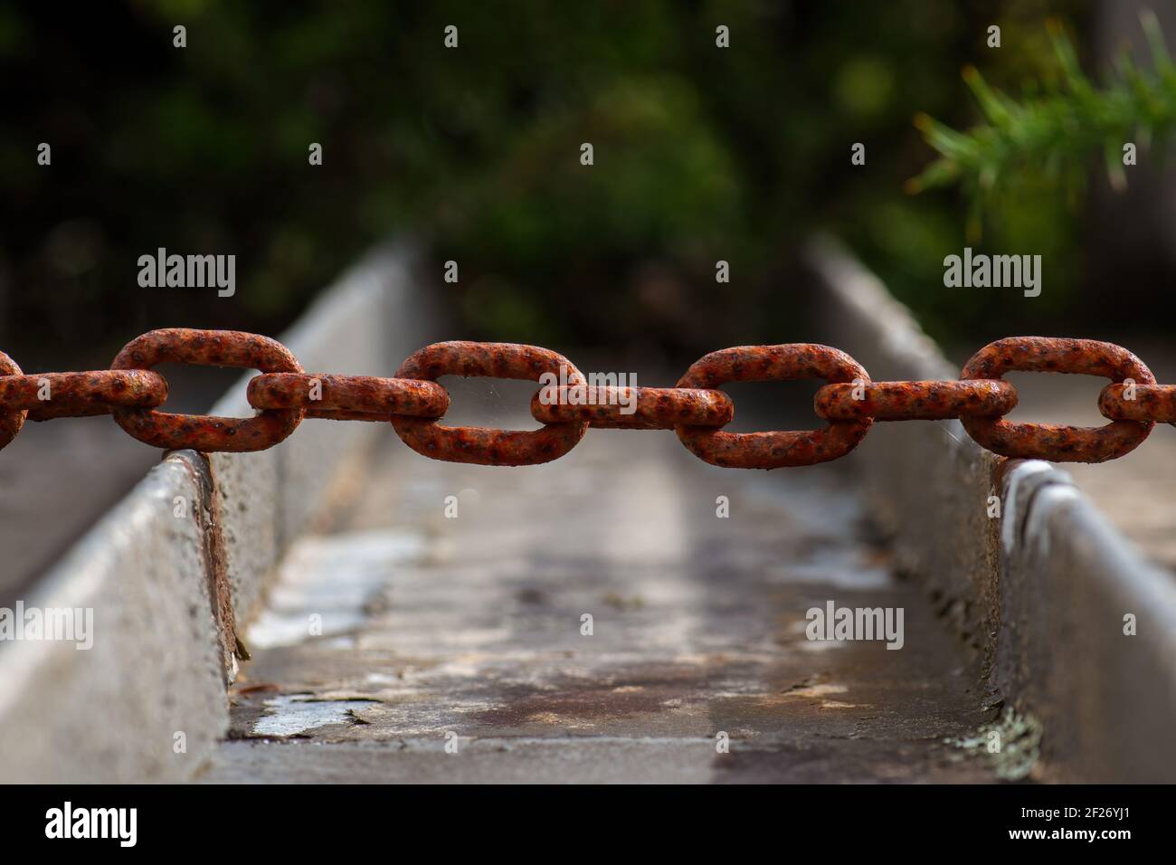 A selective focus shot of a massive rusty iron chain over a rural ...