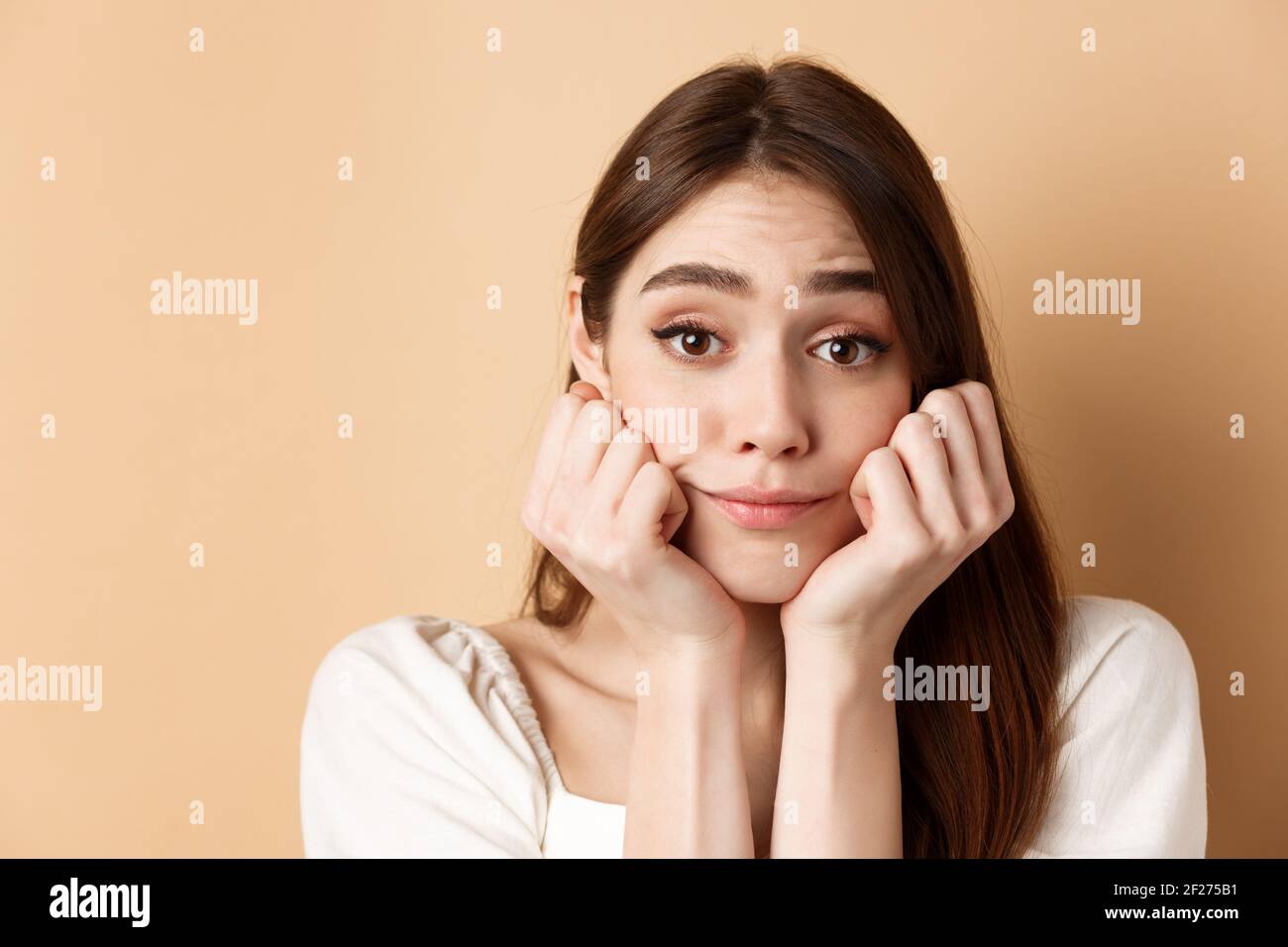 Close-up of cute and pretty girl lean face on hands, looking at camera ...