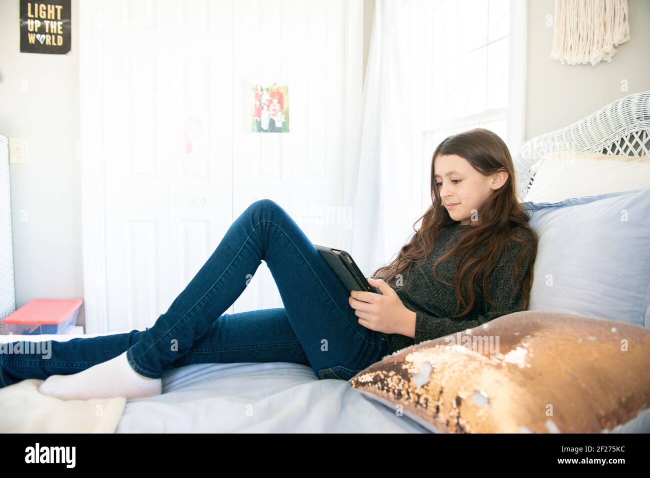 Tween girl sitting on bed with tablet in sunny bedroom Stock Photo - Alamy