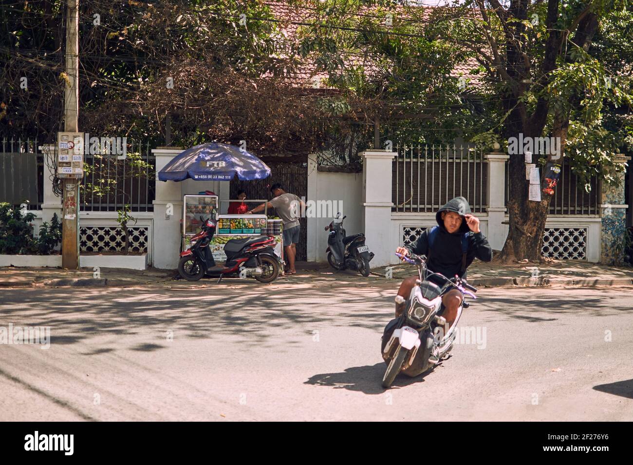 Moped driver turning around in the road, with a street vendor in the ...