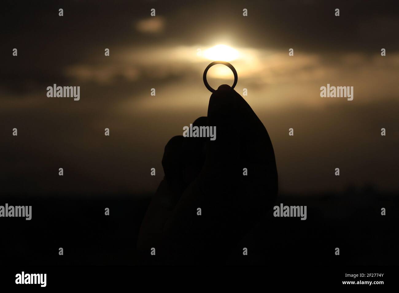 a silhouette of a hand holding a ring against the golden clouds and sun ...