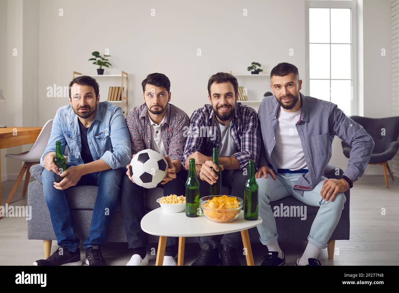 Men friends sitting together on sofa with soccer ball beer and snacks ...
