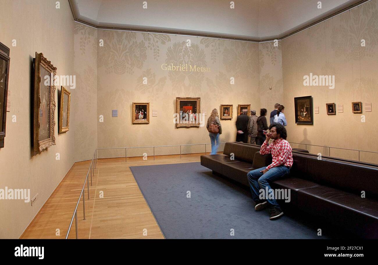 Room with paintings, standing visitors and a sitting visitor on a couch ...