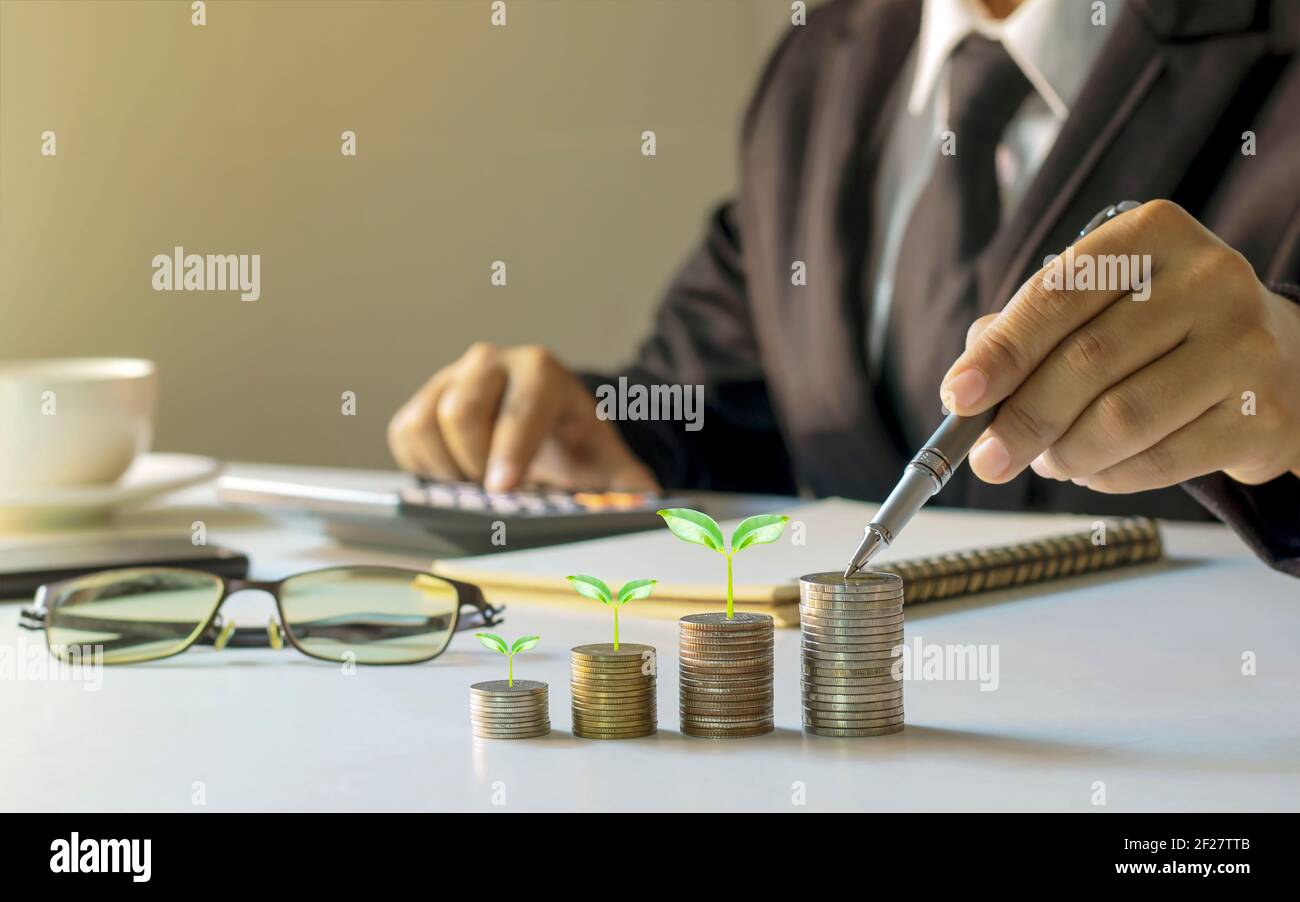 Businessman holding a pen and a tree growing on a coin, planning ideas ...