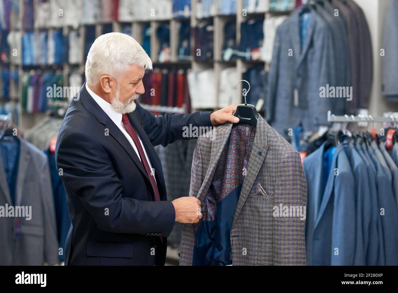 Close up of senior man choosing variety fashionable costumes in store ...