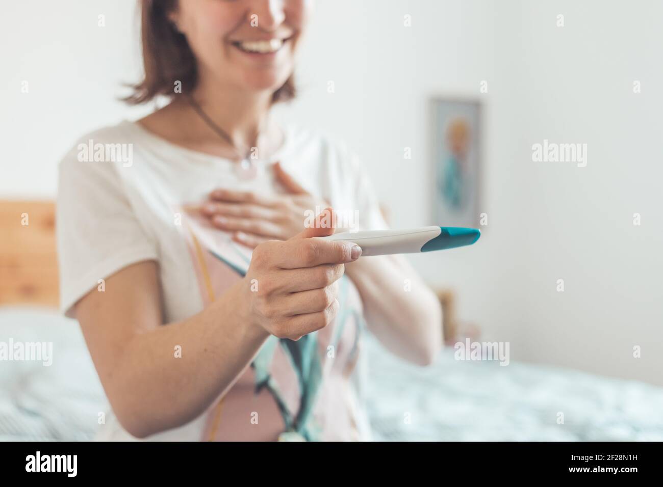 Happy woman sitting on the bed, checking pregnancy test. Result ...