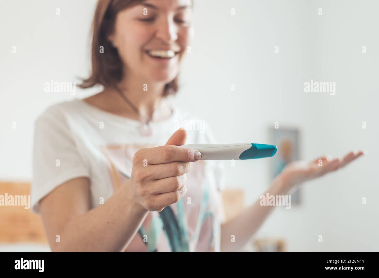 Happy woman sitting on the bed, checking pregnancy test. Result ...