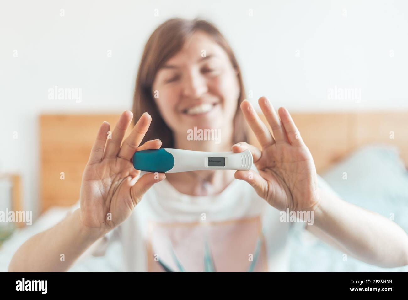 Happy woman sitting on the bed, checking pregnancy test. Result ...