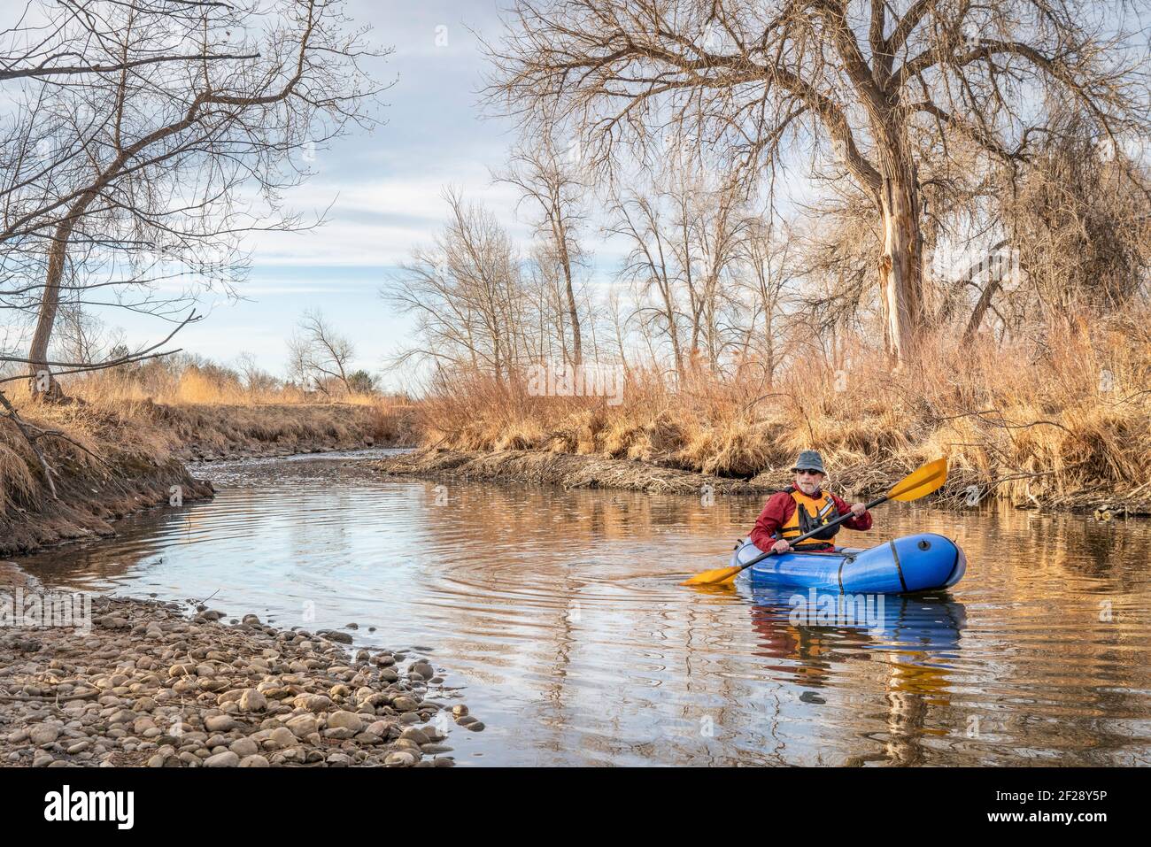 senior male is paddling an inflatable packraft on a river in early ...