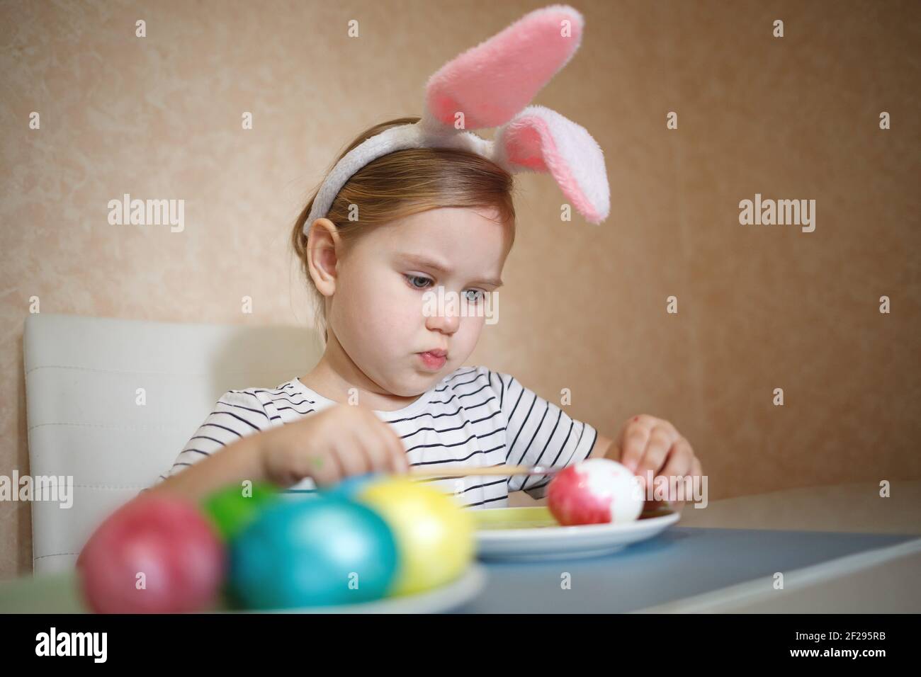 little cute blue-eyed girl in bunny ears paints Easter eggs Stock Photo ...
