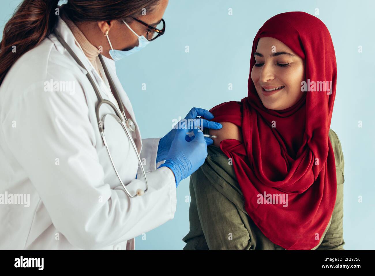 Female doctor giving vaccine injection on arm of a muslim female. Woman ...