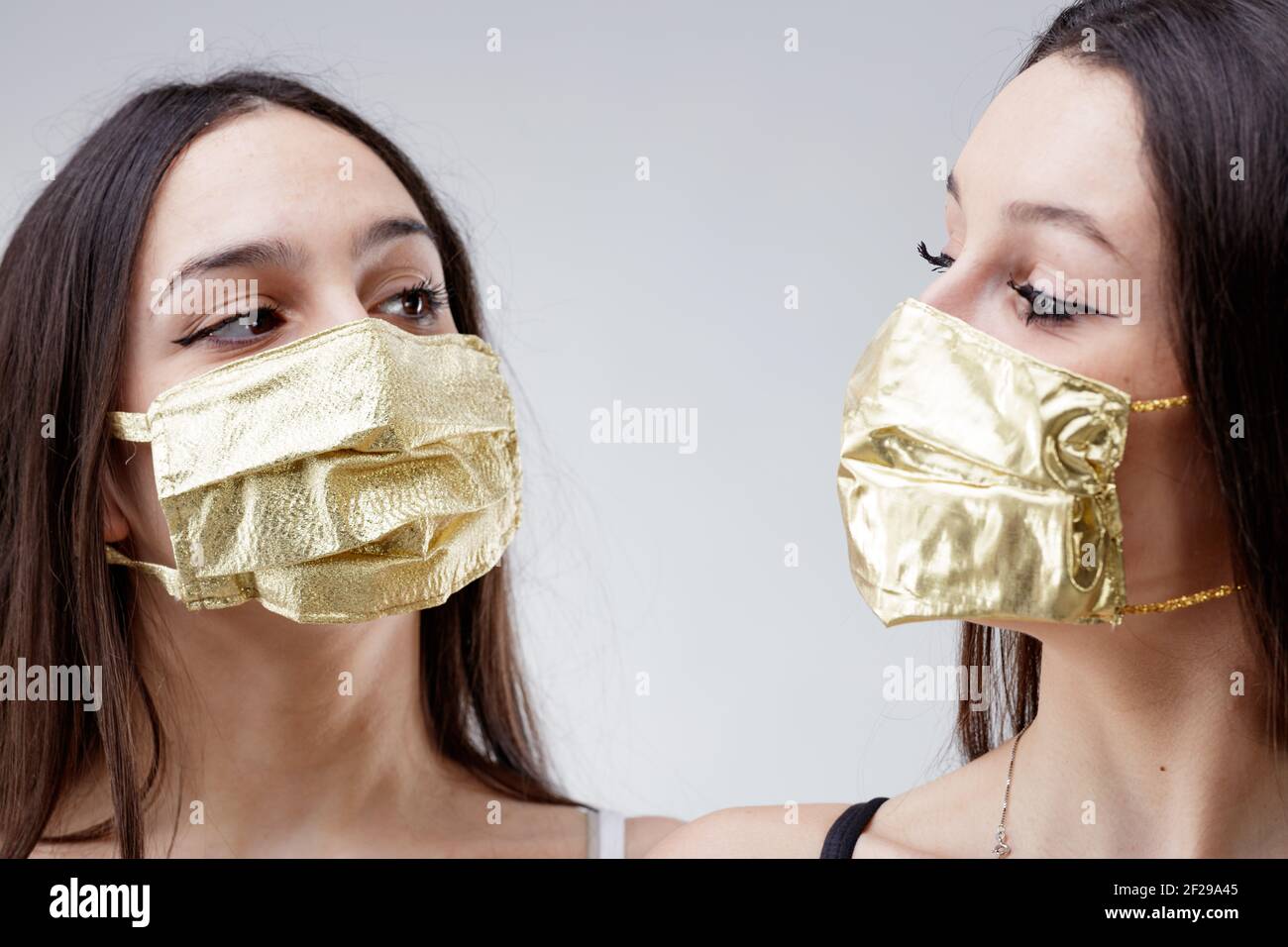 women wearing GOLDEN protective face masks staring each other, young ...