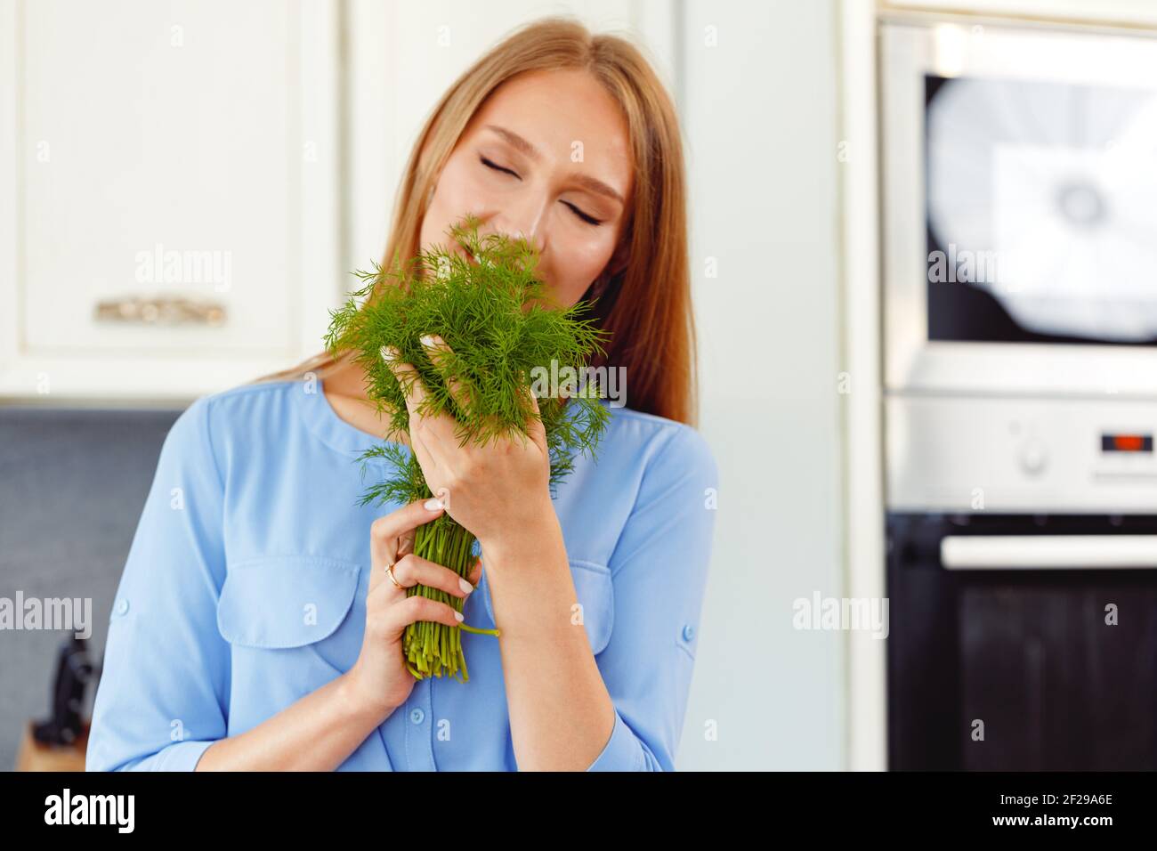 Funny woman smelling a bundle of parsley in kitchen Stock Photo - Alamy