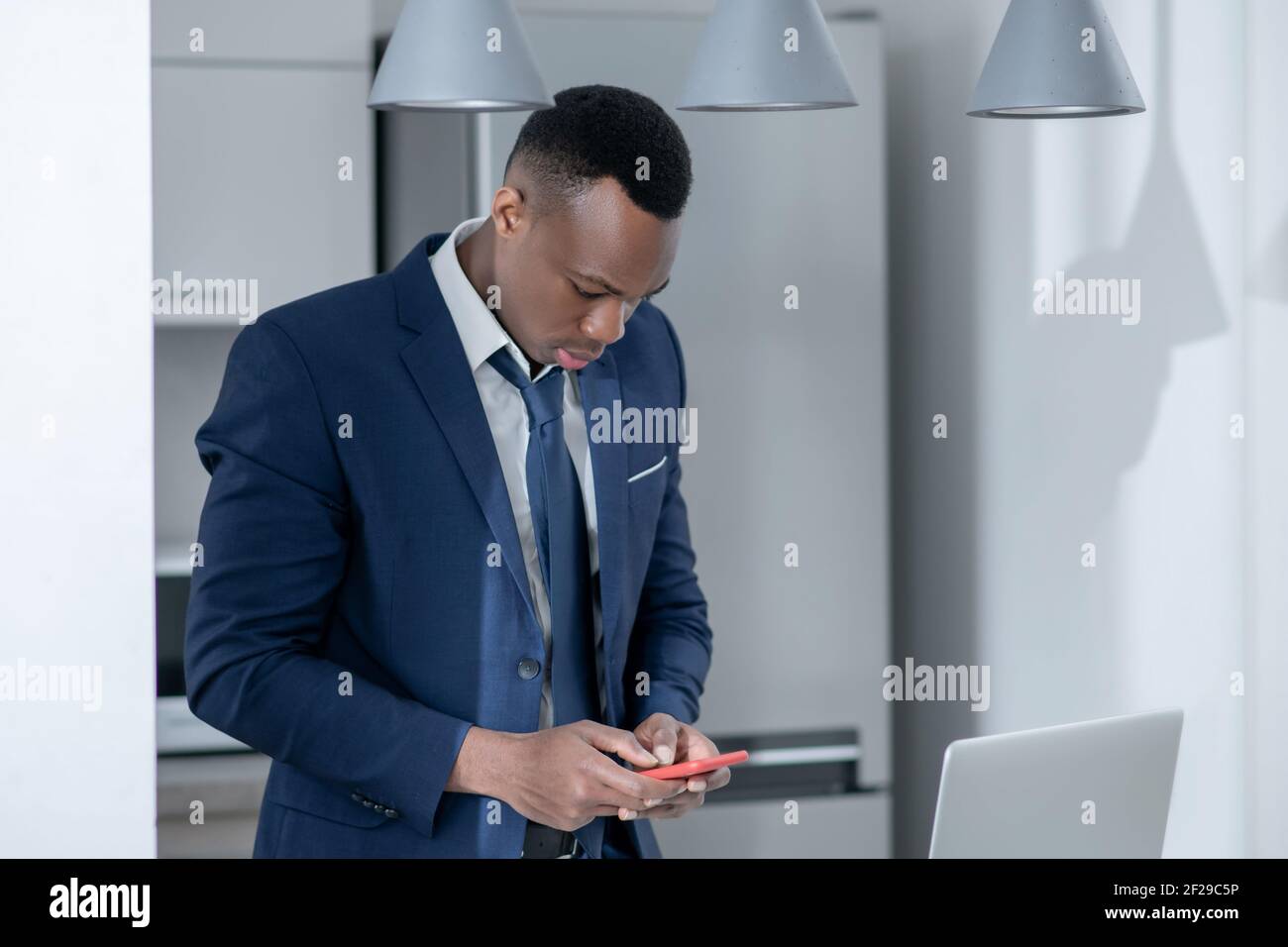 Elegant dark-skinned man reading something on laptop and looking ...