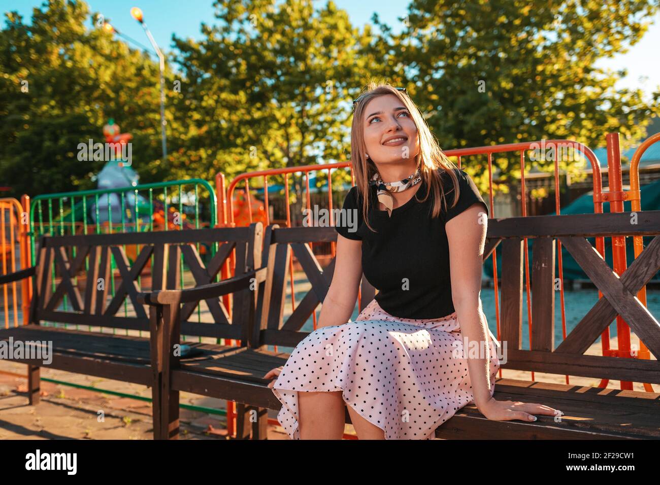 A pretty young woman is sitting on a Park bench and looking up at the ...