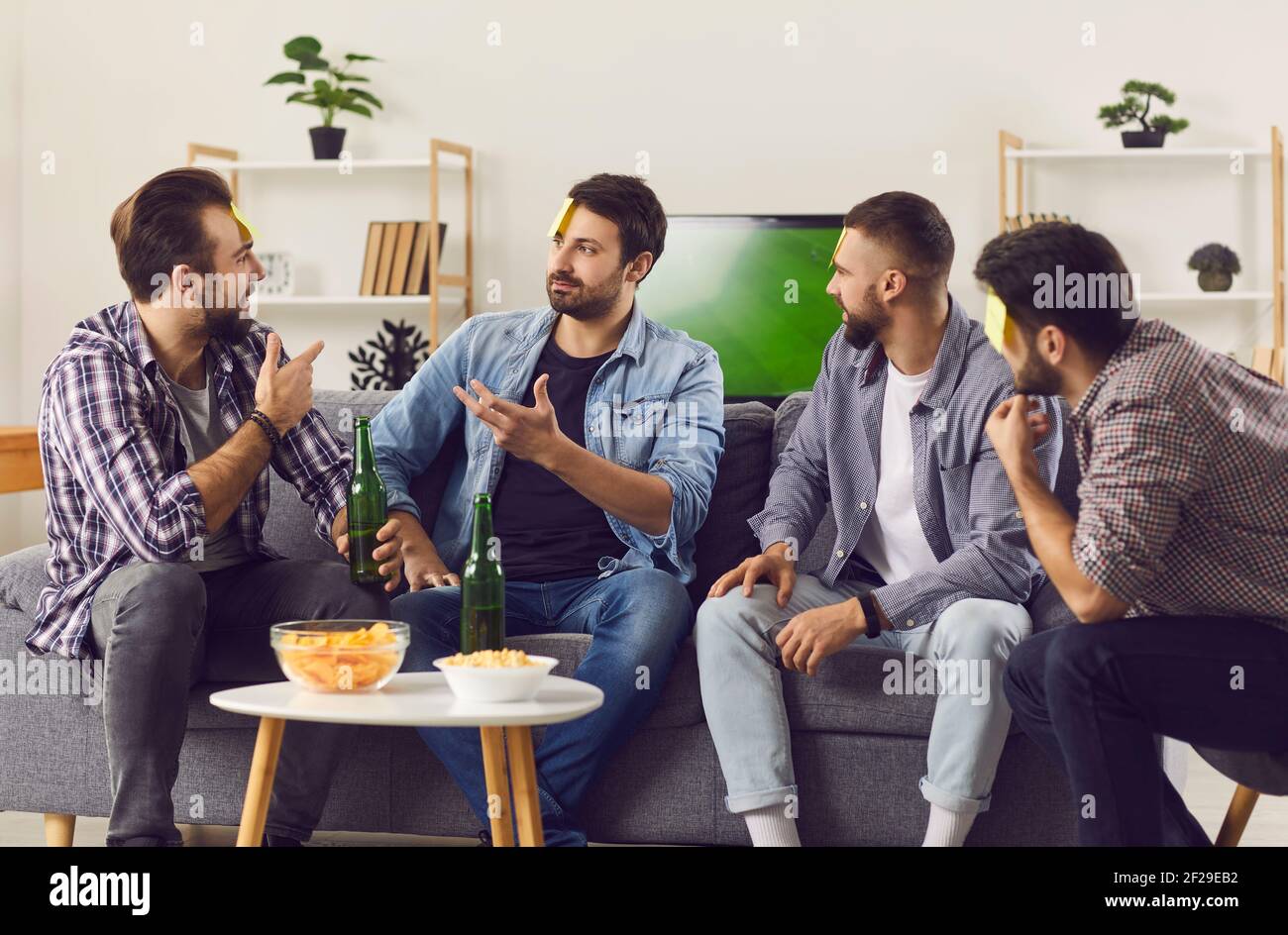 Group of friends sitting on sofa and playing Who Am I guessing game ...