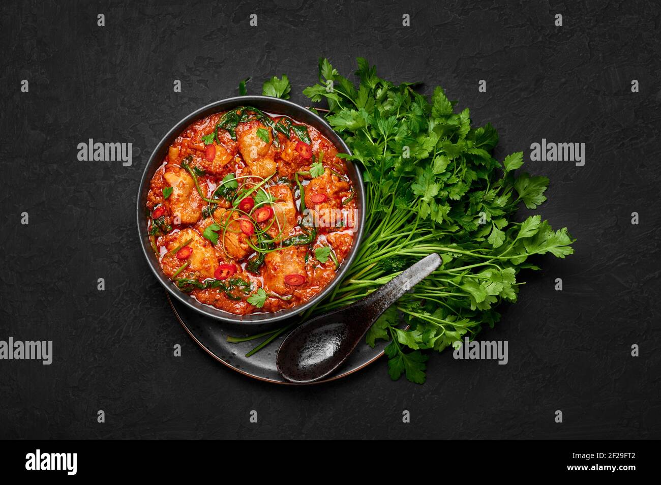 Chicken Vindaloo with spinach in black bowl on dark slate table top ...